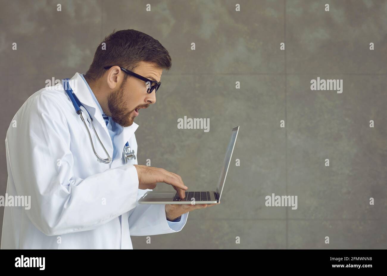 Side view of a shocked male doctor looking at a laptop screen and ...