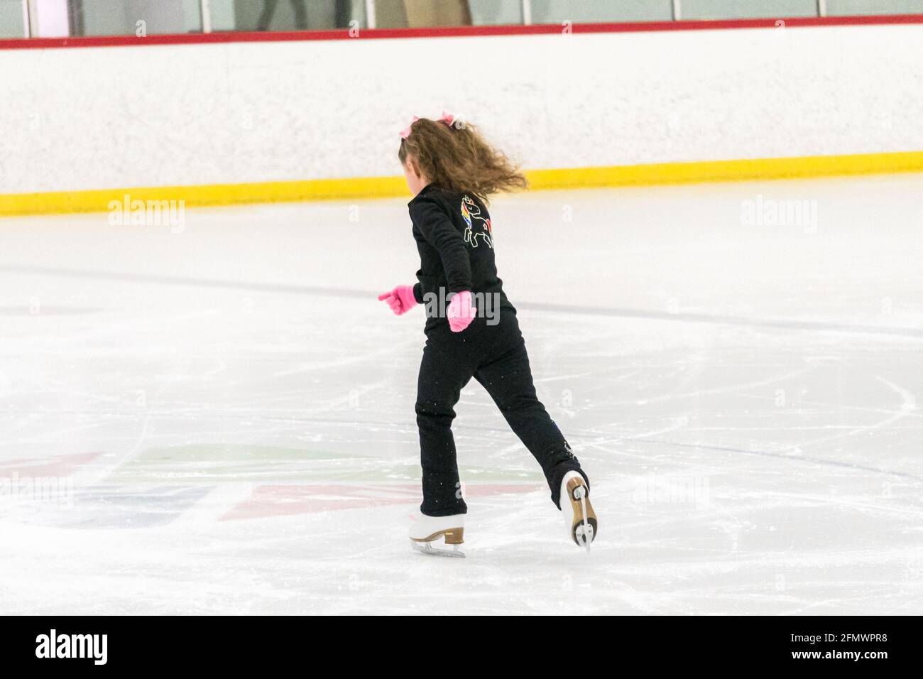 Little girl practicing figure skating moves on the indoor ice rink ...