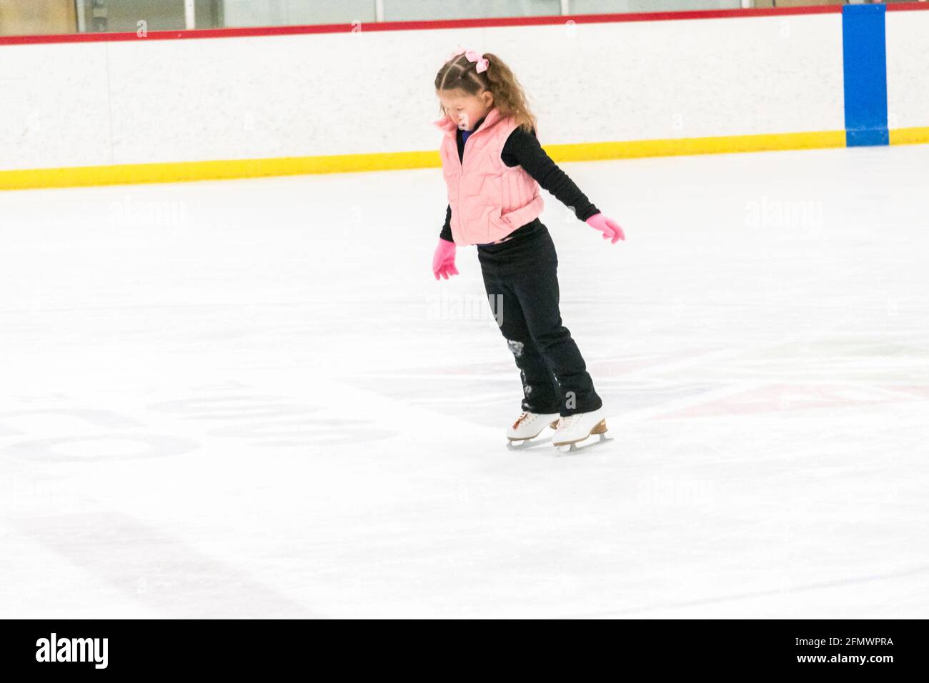Little girl practicing figure skating moves on the indoor ice rink ...