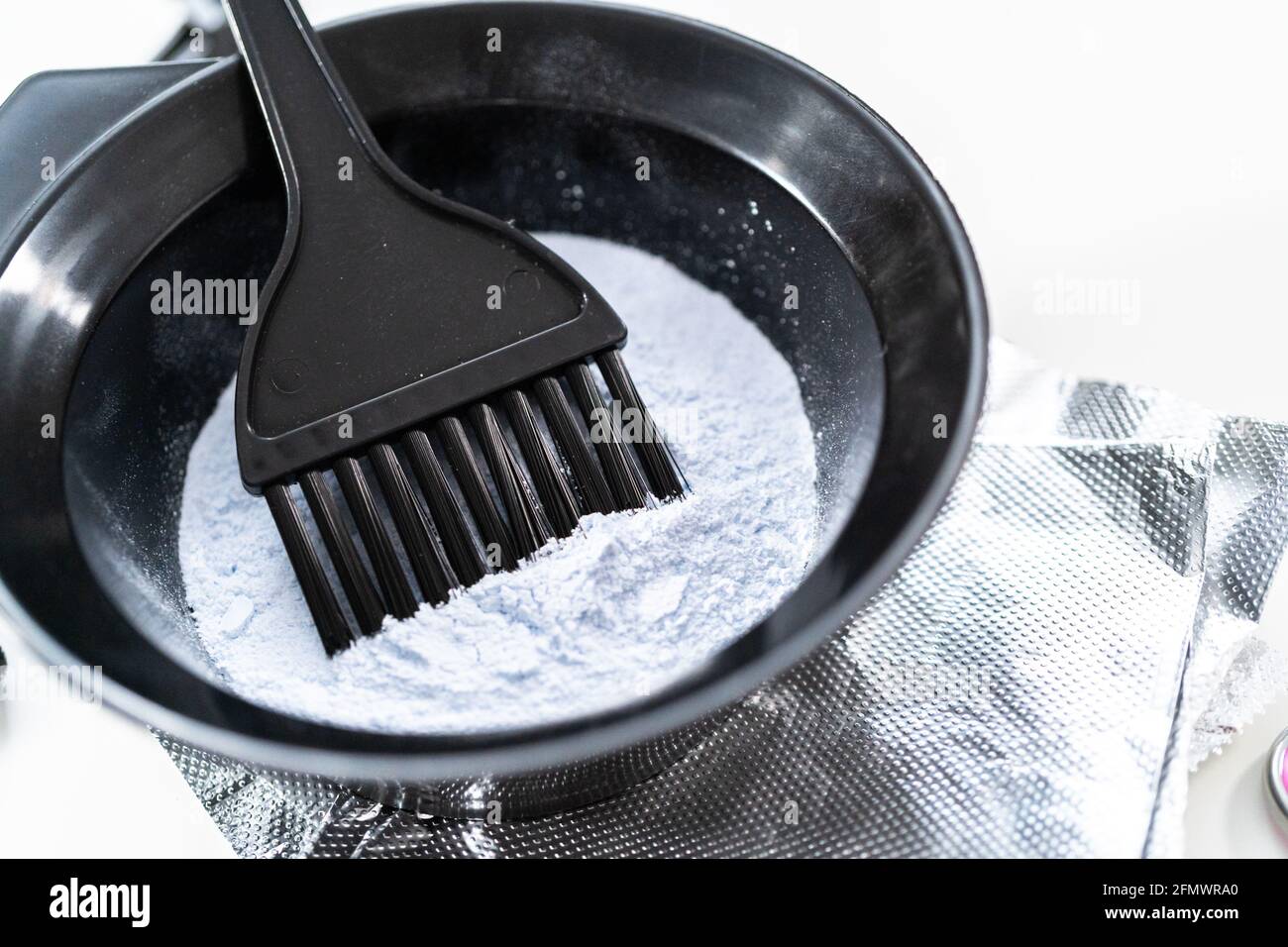 Hair color dye powder in a black plastic mixing bowl on a white ...