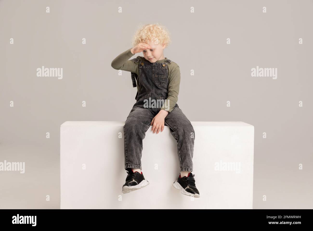 One Caucasian little boy sitting on box isolated over gray studio ...
