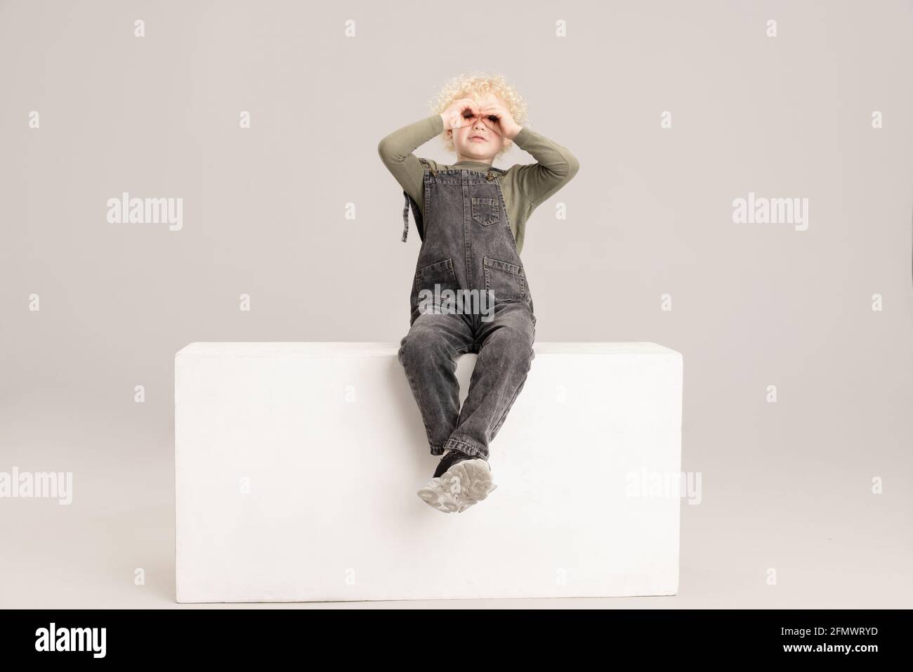 One Caucasian little boy sitting on box isolated over gray studio ...