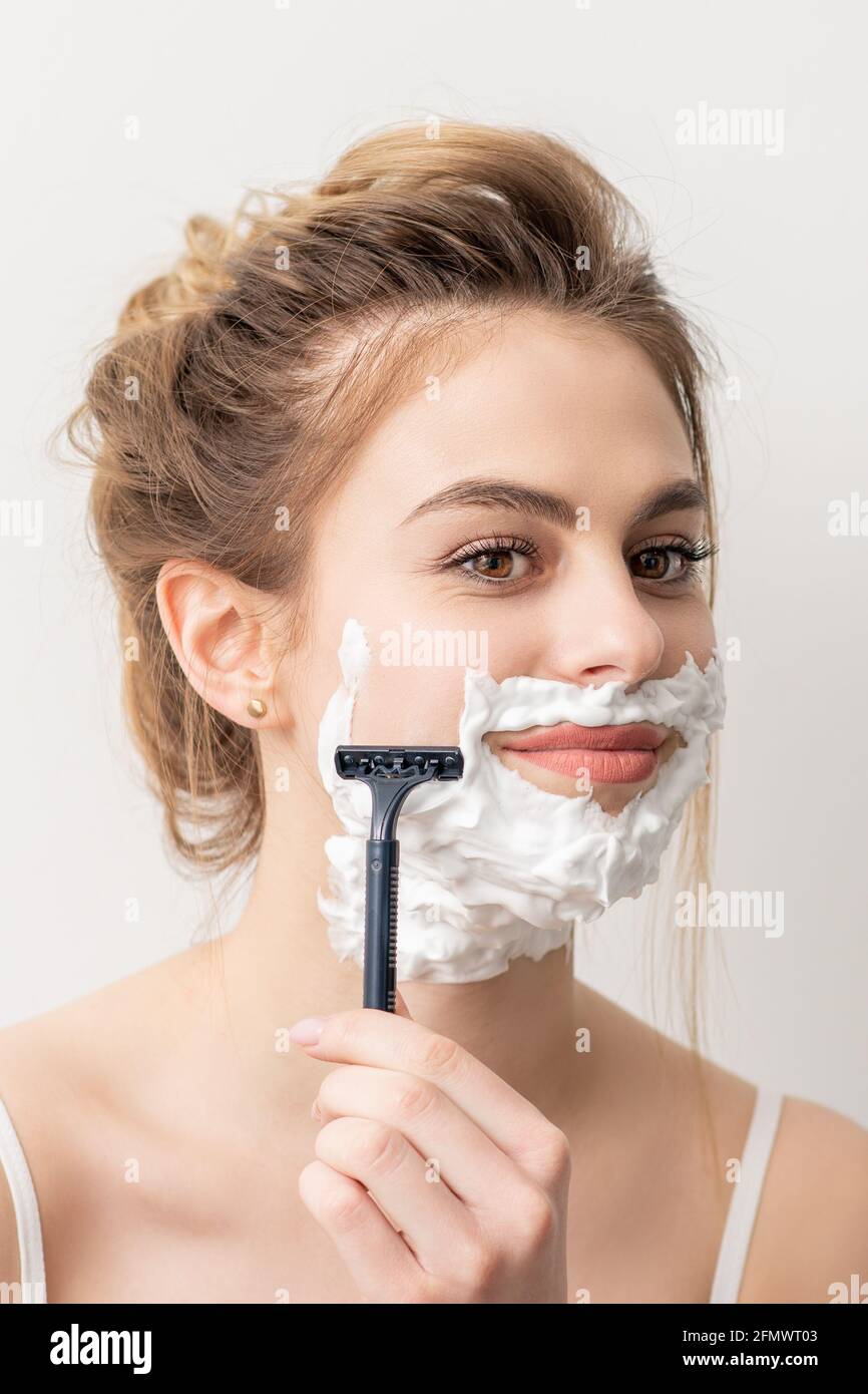 Beautiful young caucasian smiling woman shaving her face with razor on ...