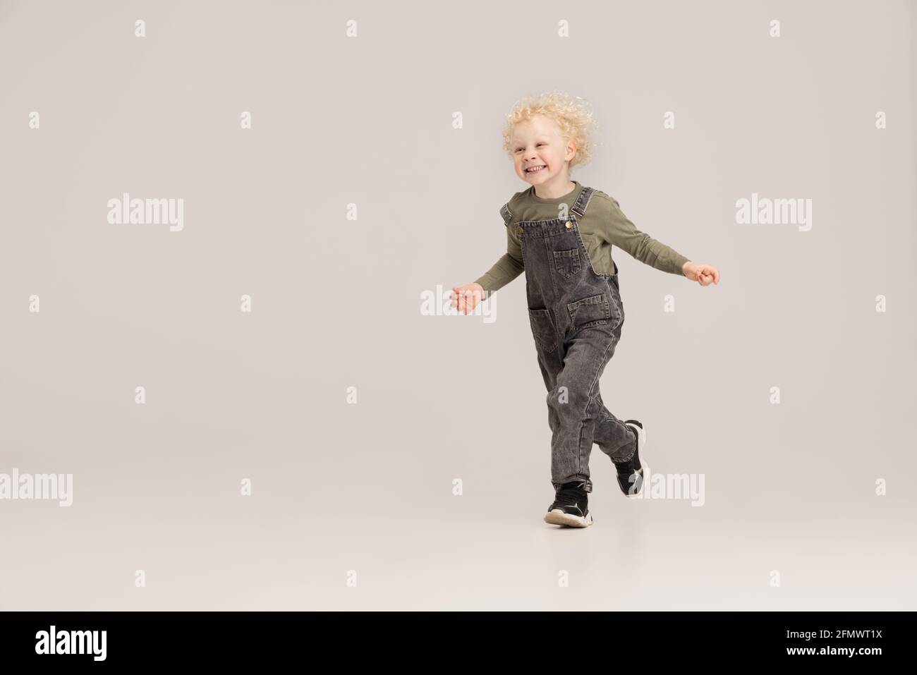 Happy Caucasian little albino boy running isolated over gray studio ...