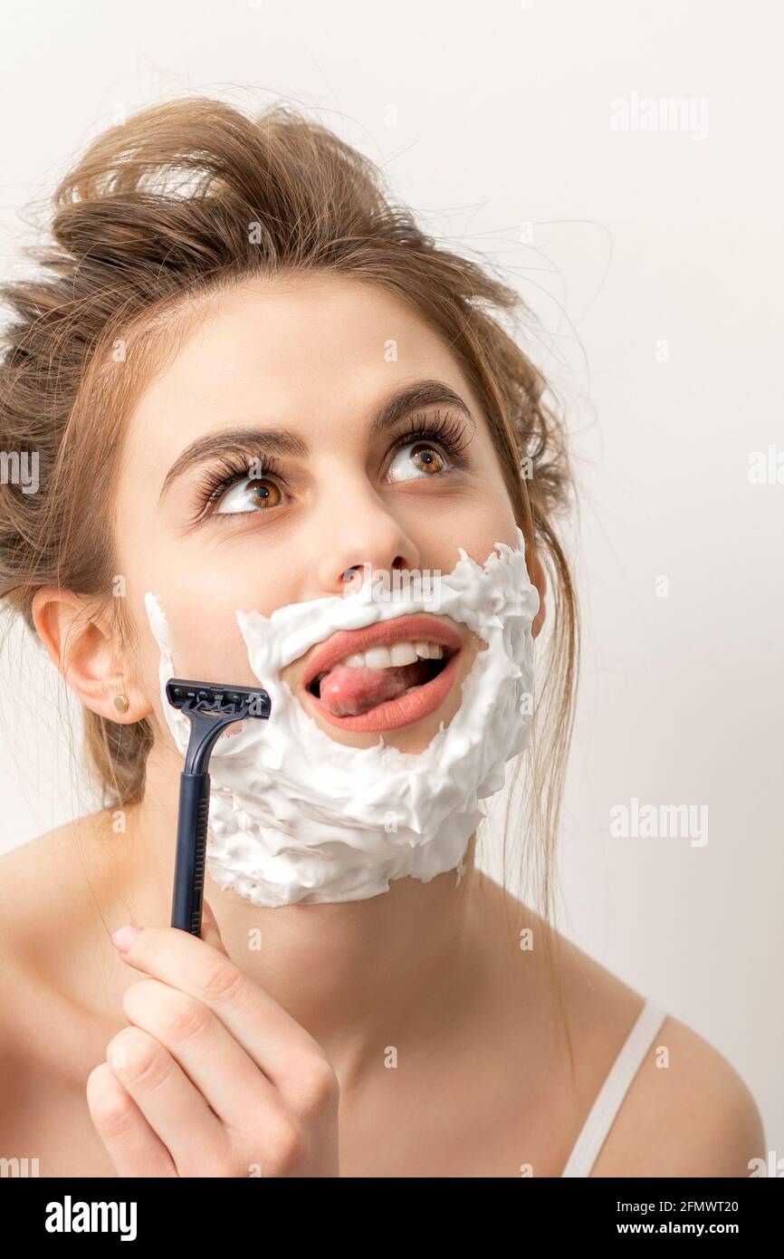 Beautiful young caucasian smiling woman shaving her face with razor ...