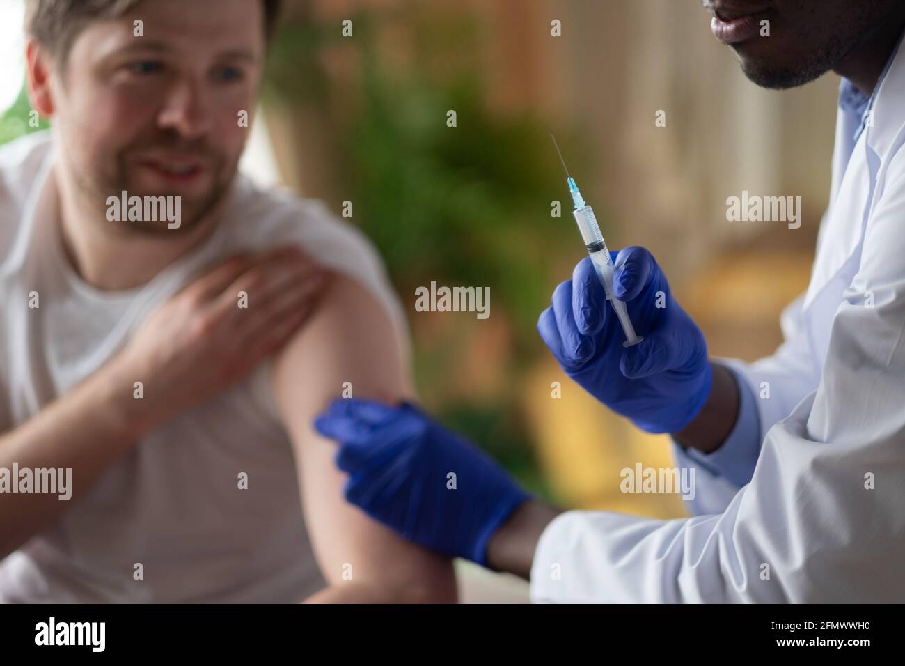 African doctor with syringe doing injection of vaccine to male patient ...
