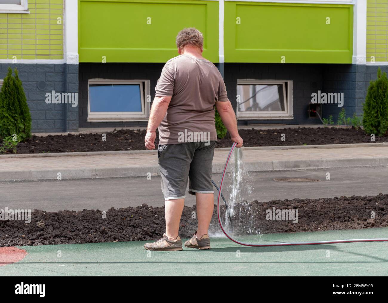 Man hosing down the ground in the heat outside his home. Man watering ...