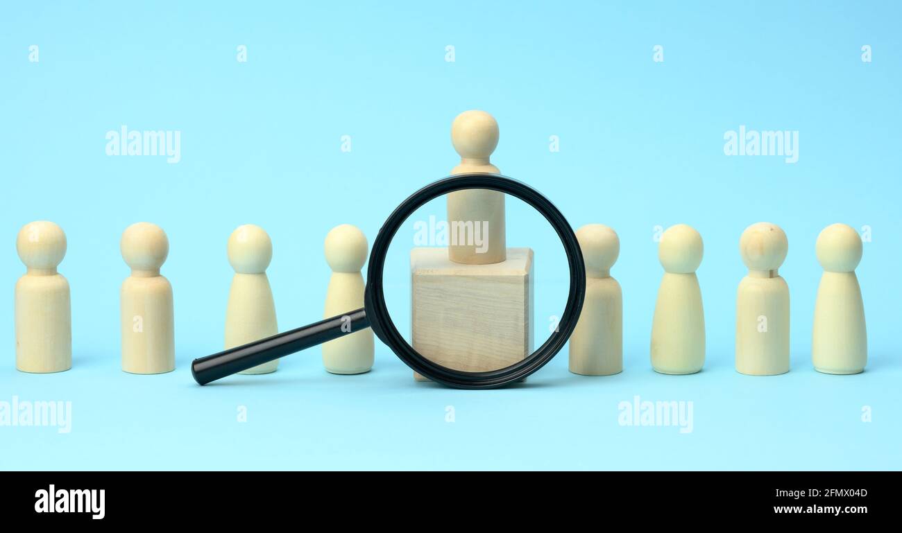 wooden figures of men stand on a blue background and a black magnifying ...