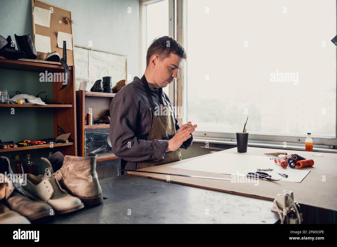A young shoemaker makes a drawing for a pattern for leather shoes on a ...