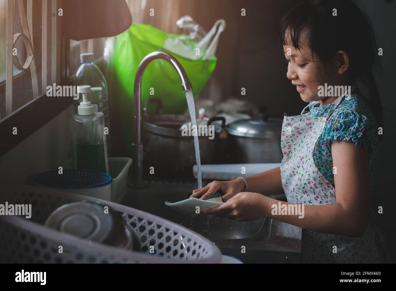 Asian little child girl washing dishes in the kitchen with smile and ...