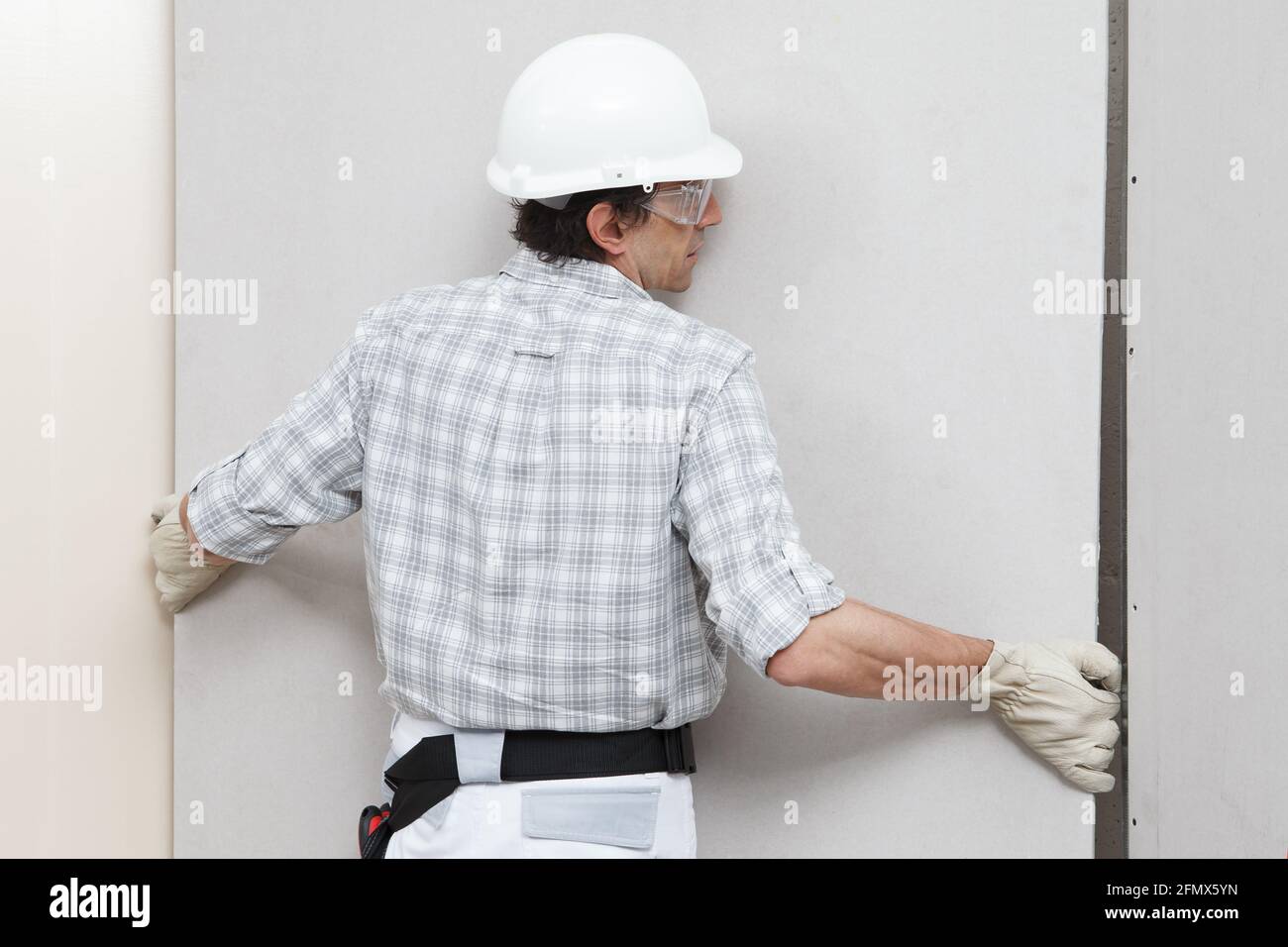 man drywall worker installing plasterboard sheet to wall. Wearing ...