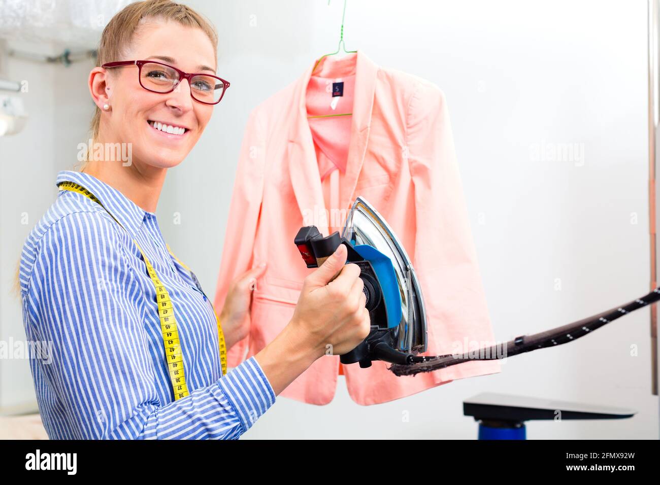 Female cleaner in laundry shop or textile dry-cleaning ironing jacket ...