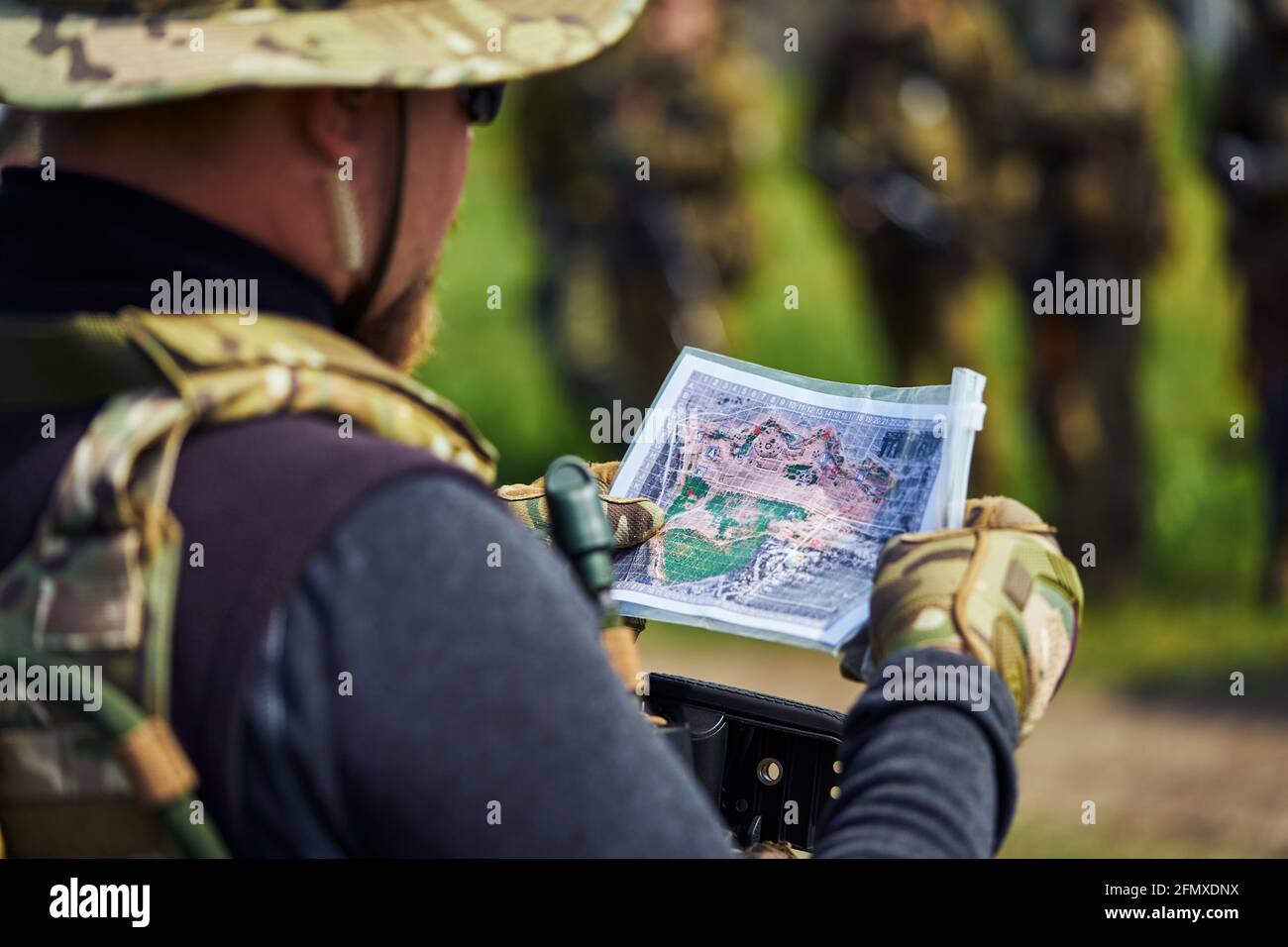 Close-up shot of an airsoft player in military uniform examining a map ...