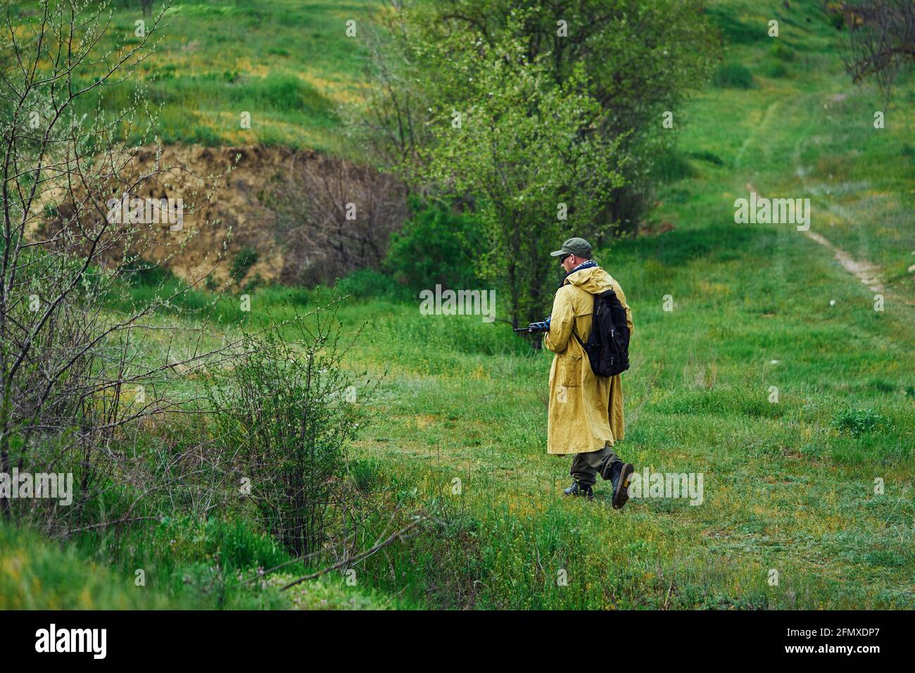 An airsoft player in a yellow raincoat walks across the field with a ...