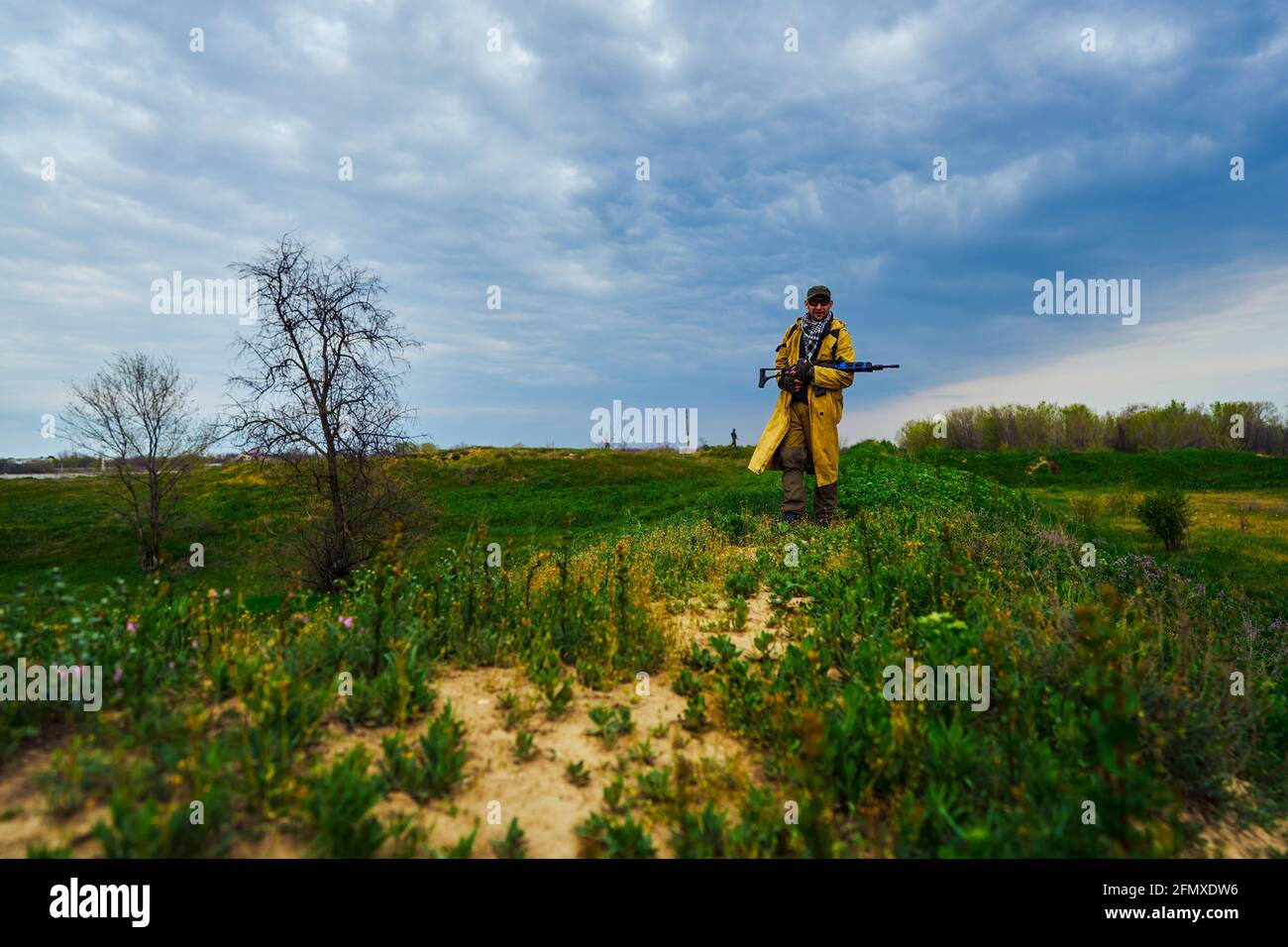 An airsoft player in a yellow raincoat walks across the field with a ...