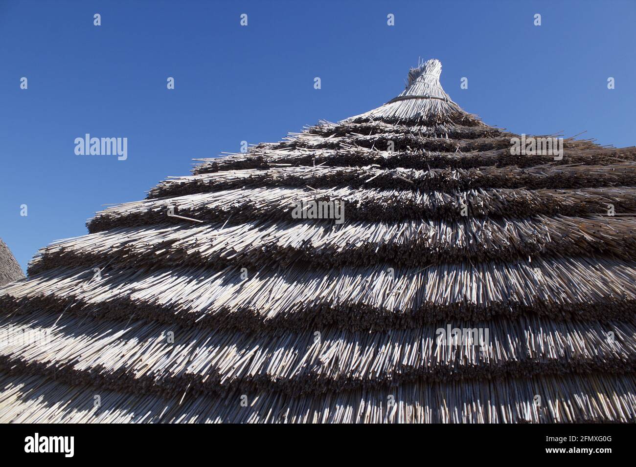 Low angle shot of straw-covered roof at a round hut against a blue sky ...