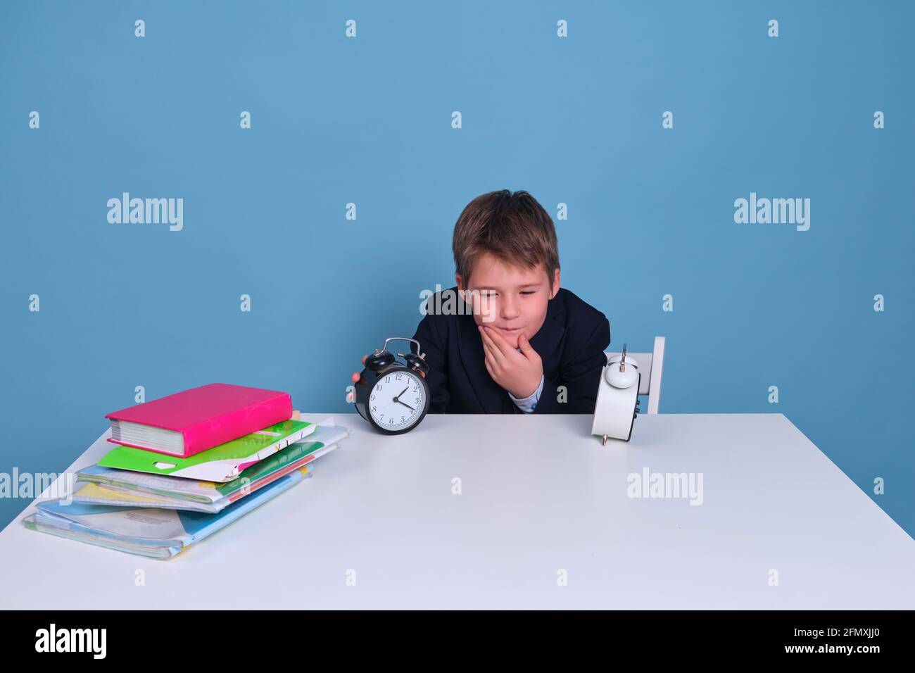 Boy schoolboy with a alarm clock in his hands at the table on a blue ...