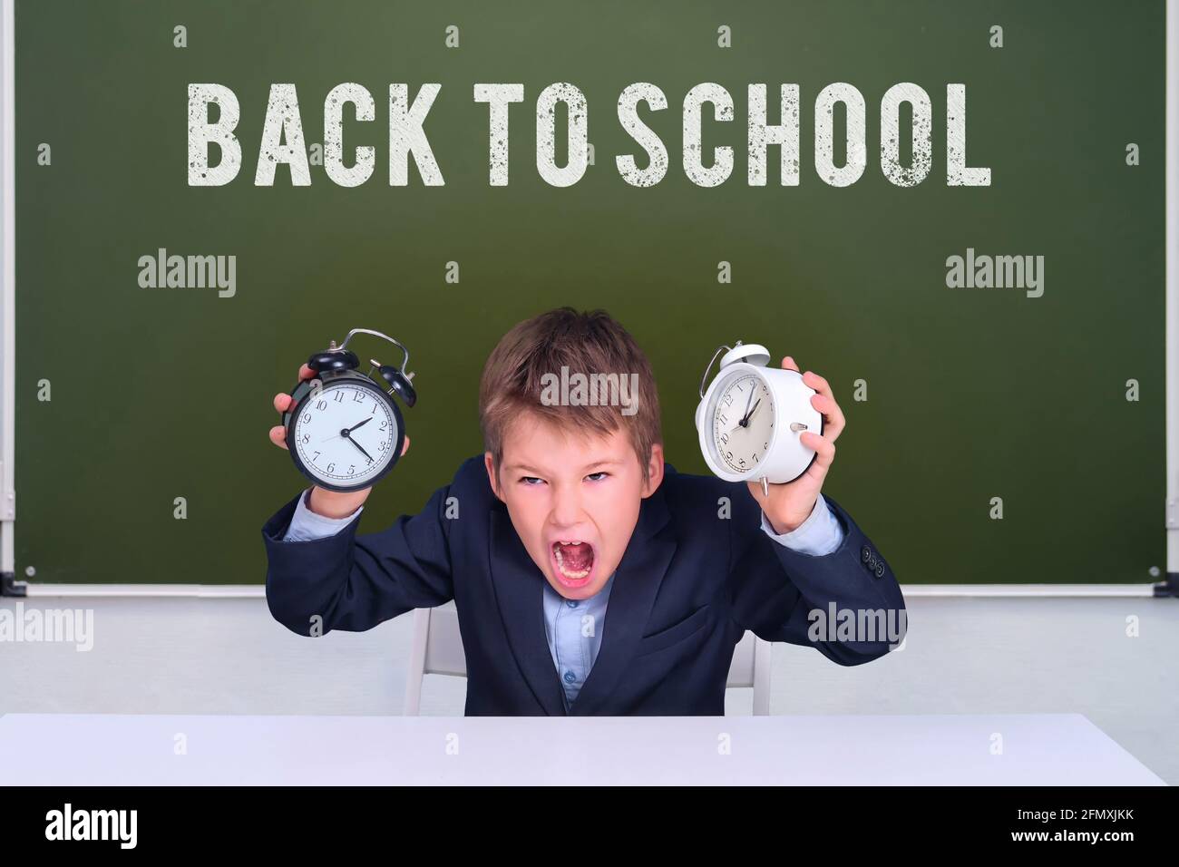Schoolboy boy with two alarm clocks at the desk at the blackboard and ...