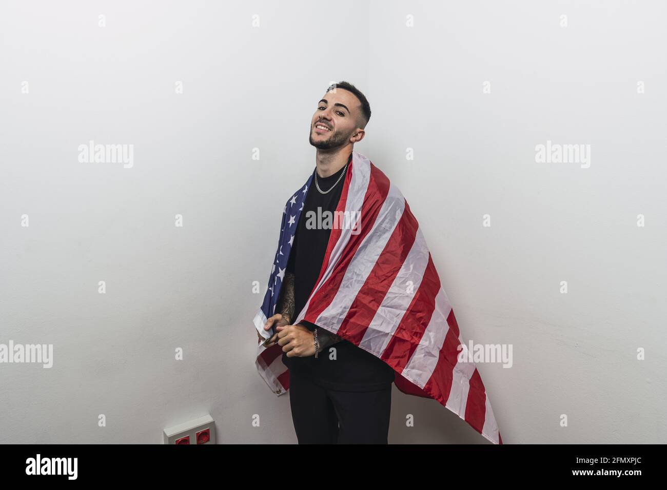 Young proud Hispanic man holding a US flag around is shoulders against ...