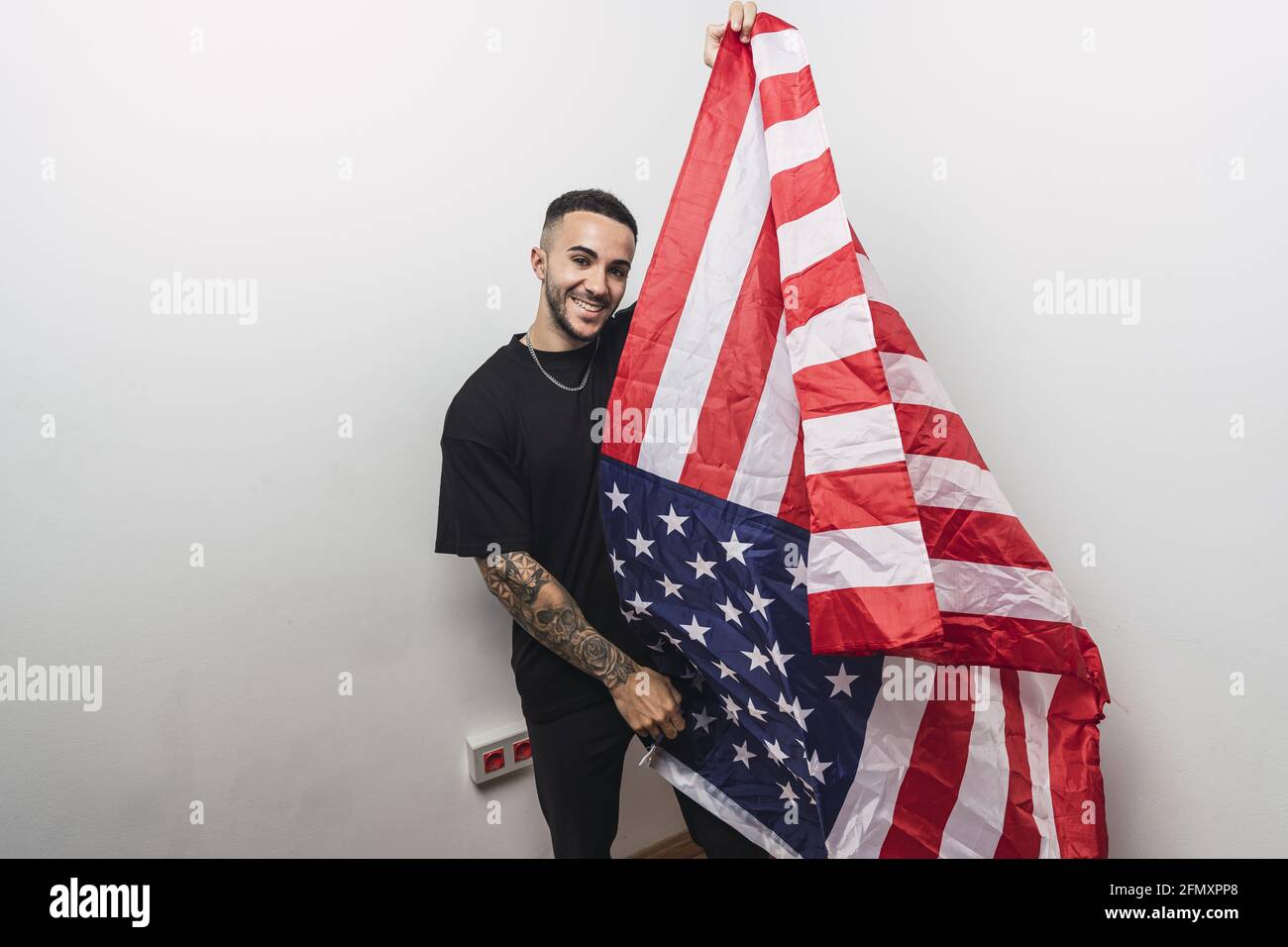 Young proud Hispanic man holding a US flag against a white background ...