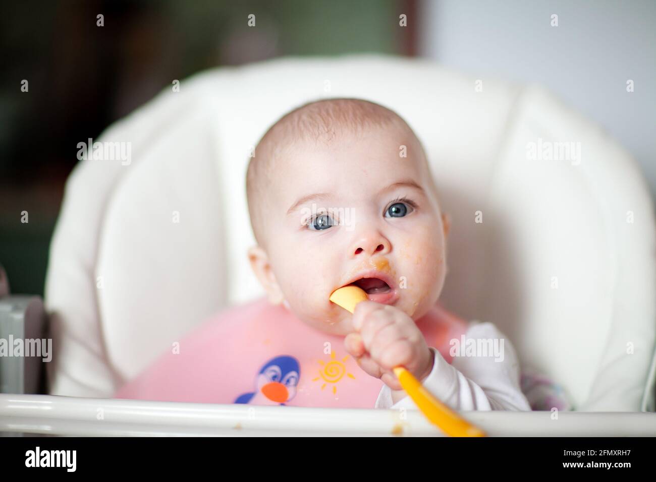 Cheerful baby child eats food itself with spoon. Portrait of happy kid ...