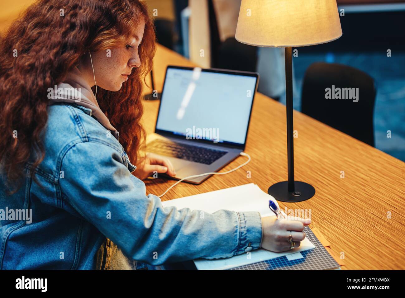 Female student writing in her notebook while studying in library. Girl ...