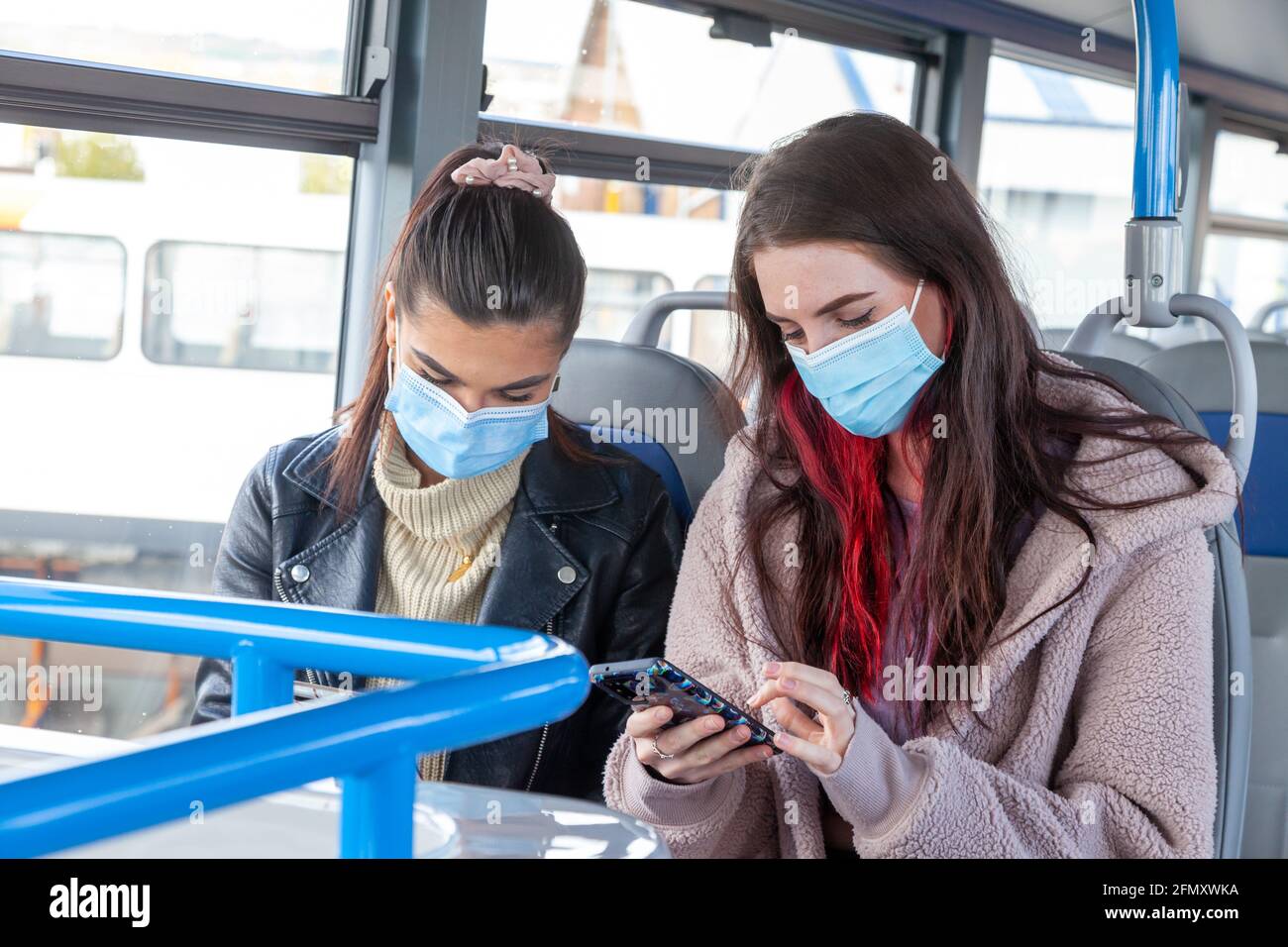 Two young women sitting on a bus using their phones Stock Photo - Alamy