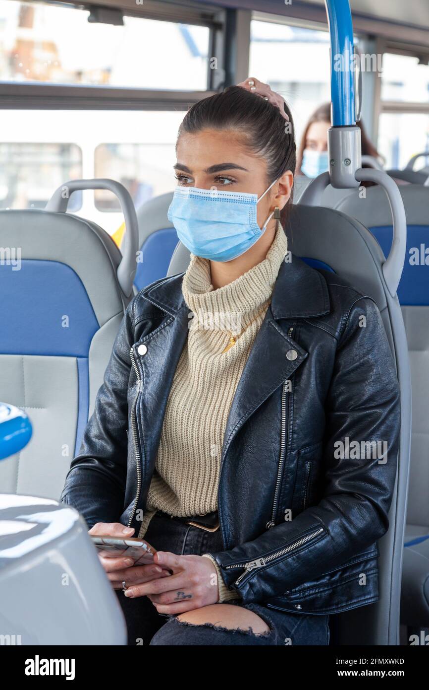 A young woman sitting looking forward on a bus with another passenger ...