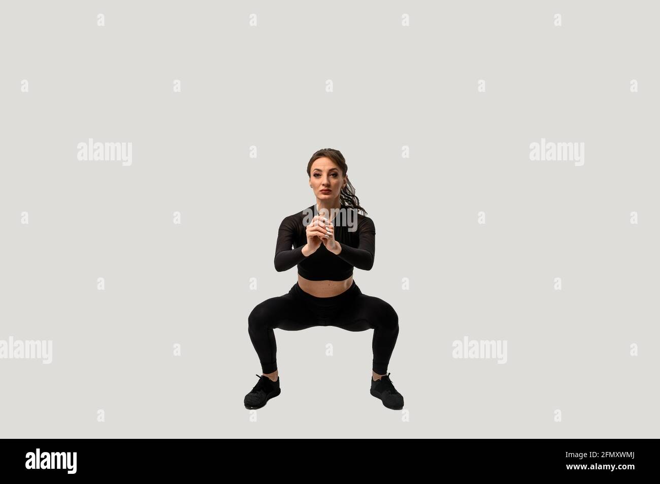 Full length portrait of a young fitness woman doing squatting isolated ...