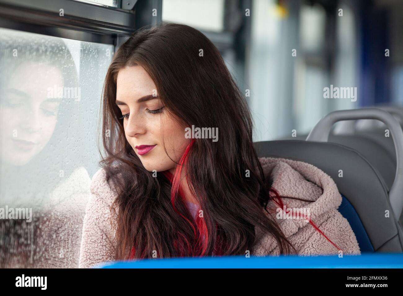 A beautiful young female student sitting on a bus with her eyes closed ...