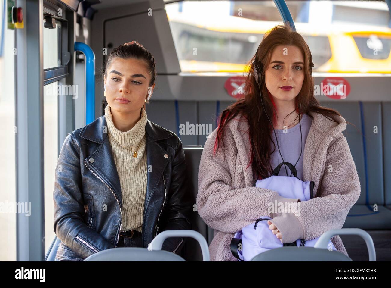 two women travelling on a bus together sitting side by side not talking ...