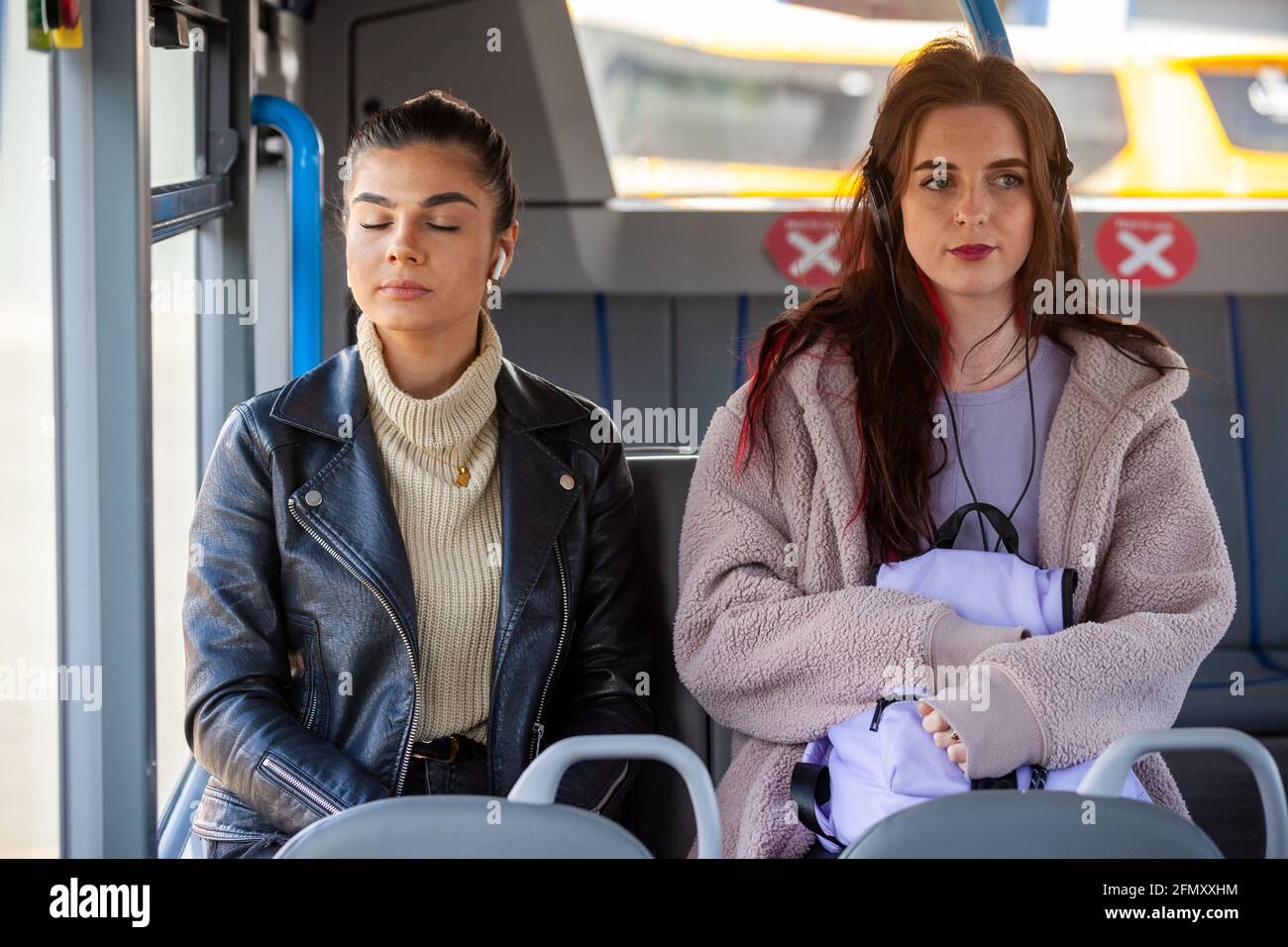 two women travelling on a bus together sitting side by side not talking ...