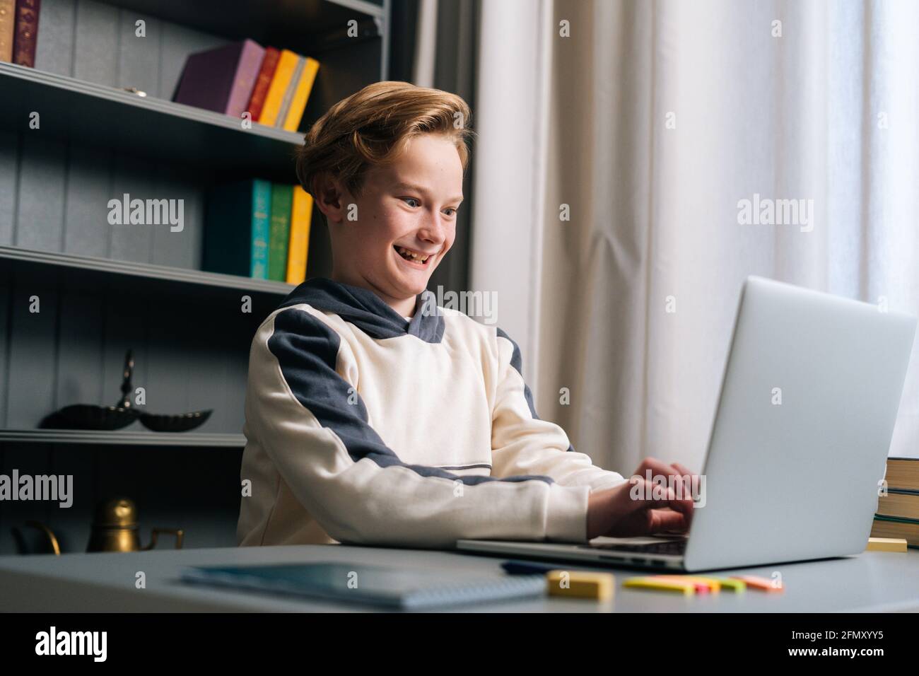 Side close-up view of cheerful child boy using typing laptop chatting ...