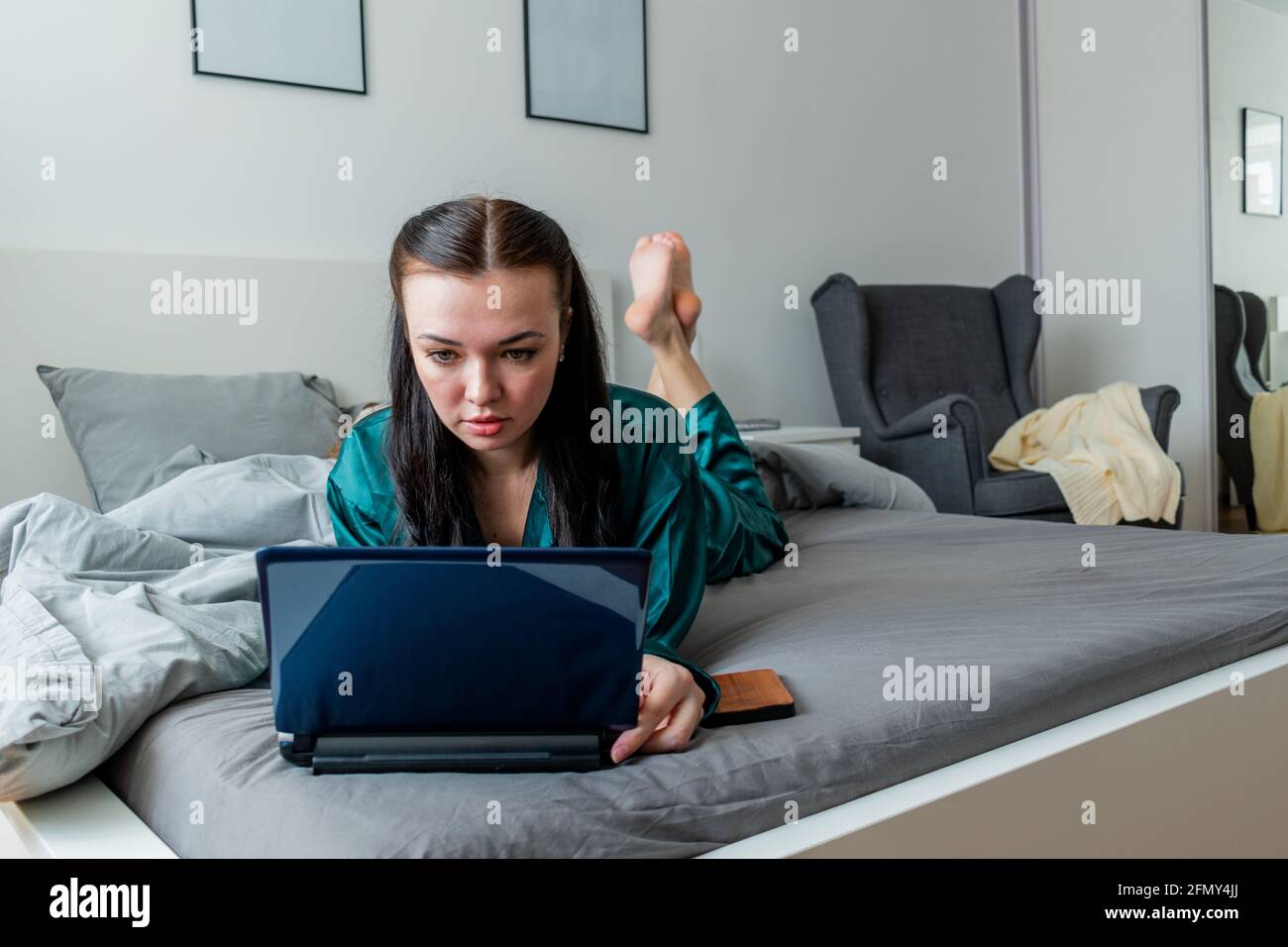Young woman work at laptop while sitting on bed in bedroom. Concept of ...