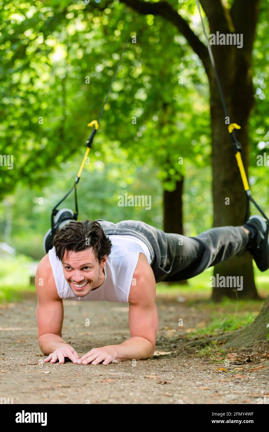 man exercising with suspension trainer sling in City Park under summer ...