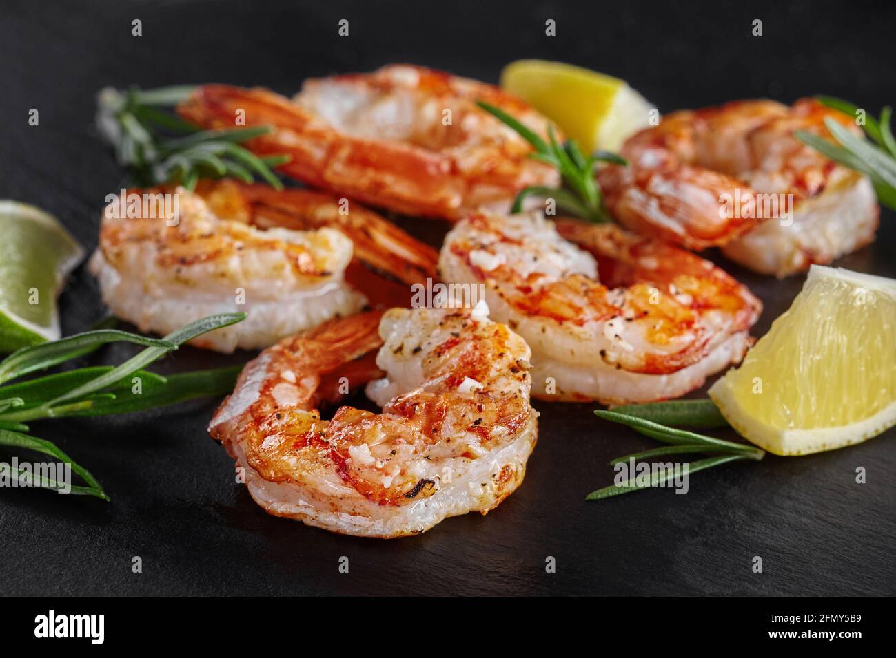 Fried scampi tails with lime, lemon and rosemary on black background ...