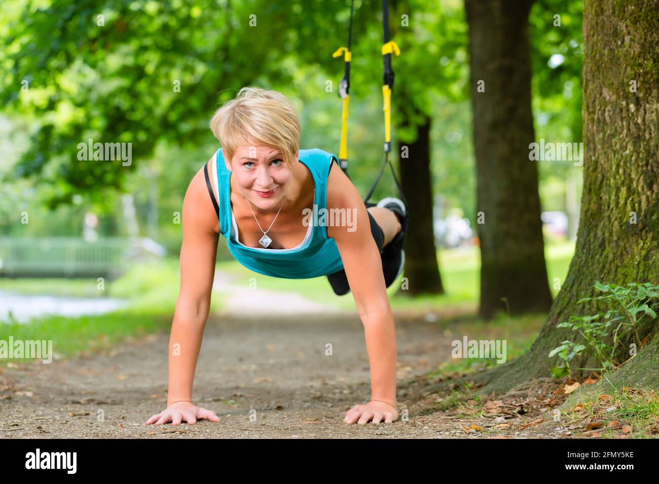 Young woman exercising with suspension trainer sling in City Park under ...