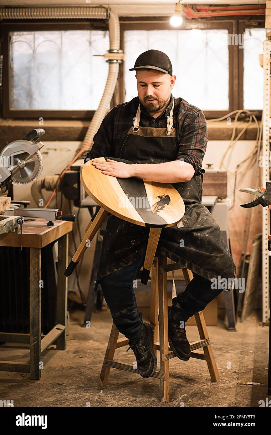carpenter examines table of his production in carpentry workshop Stock ...