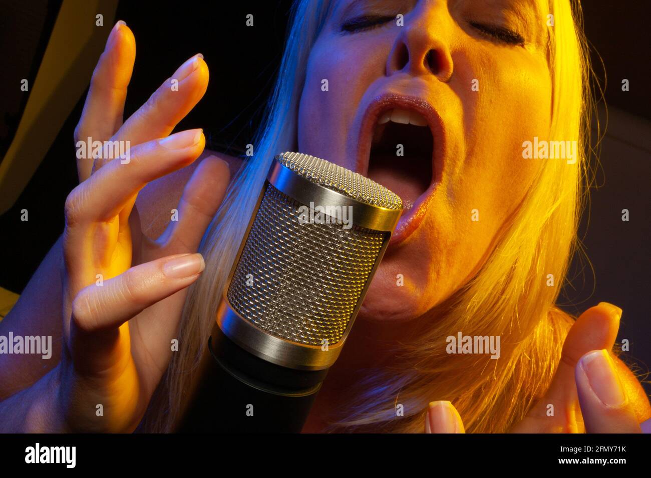 Female vocalist under gelled lighting sings with passion into condenser ...
