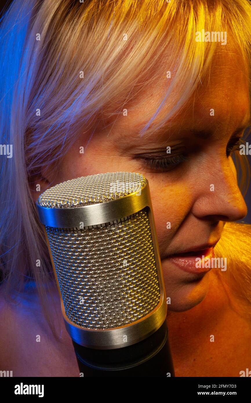 Female vocalist under gelled lighting sings with passion into condenser ...