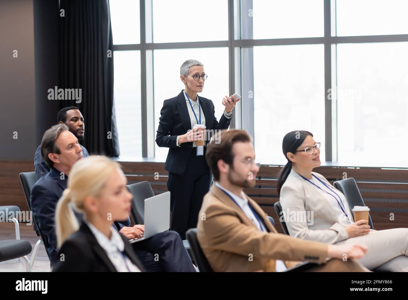 Businesswoman with cellphone and takeaway drink talking near ...