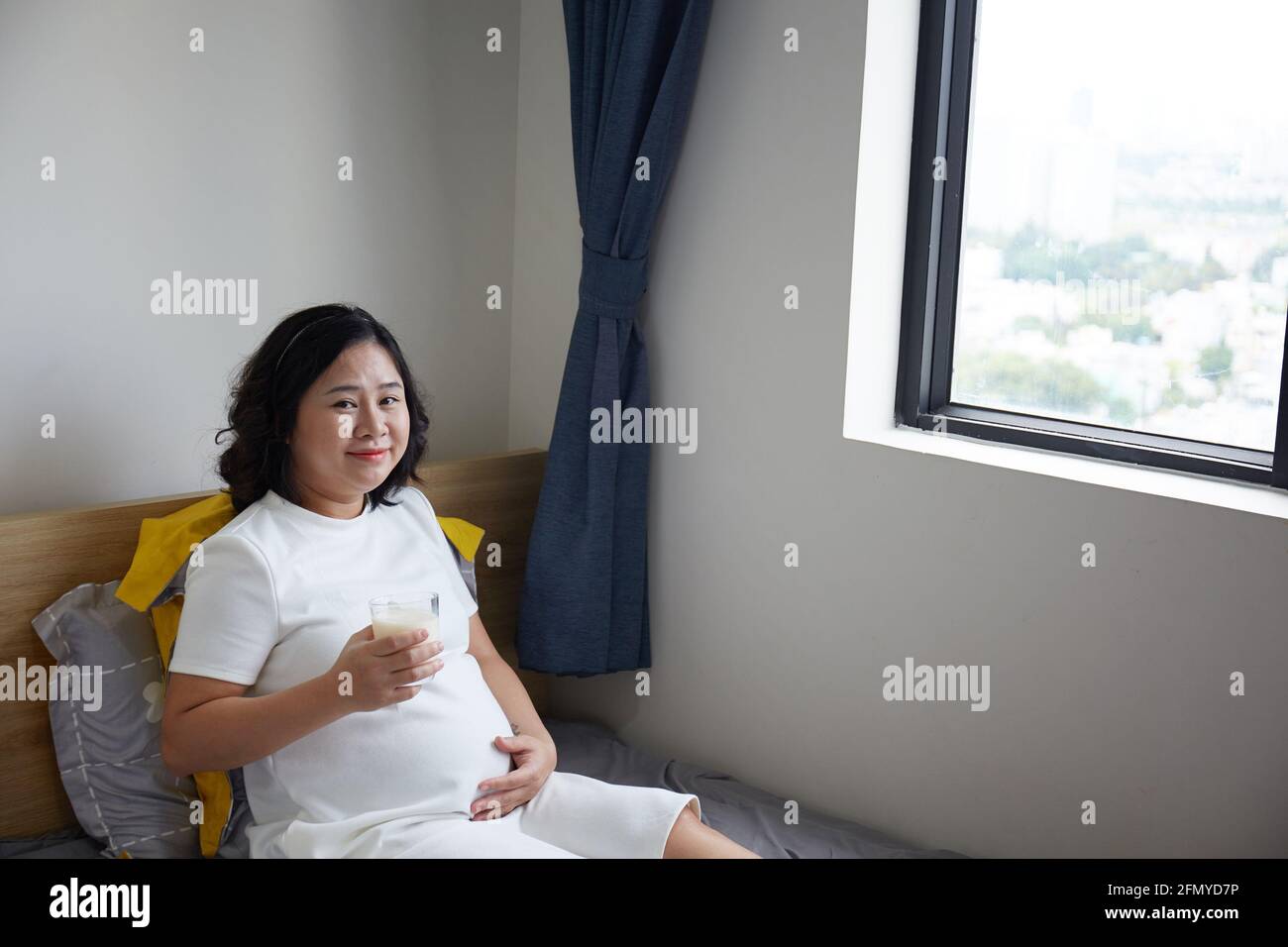 Closeup shot of a Southeast Asian pregnant female in a white dress on a ...