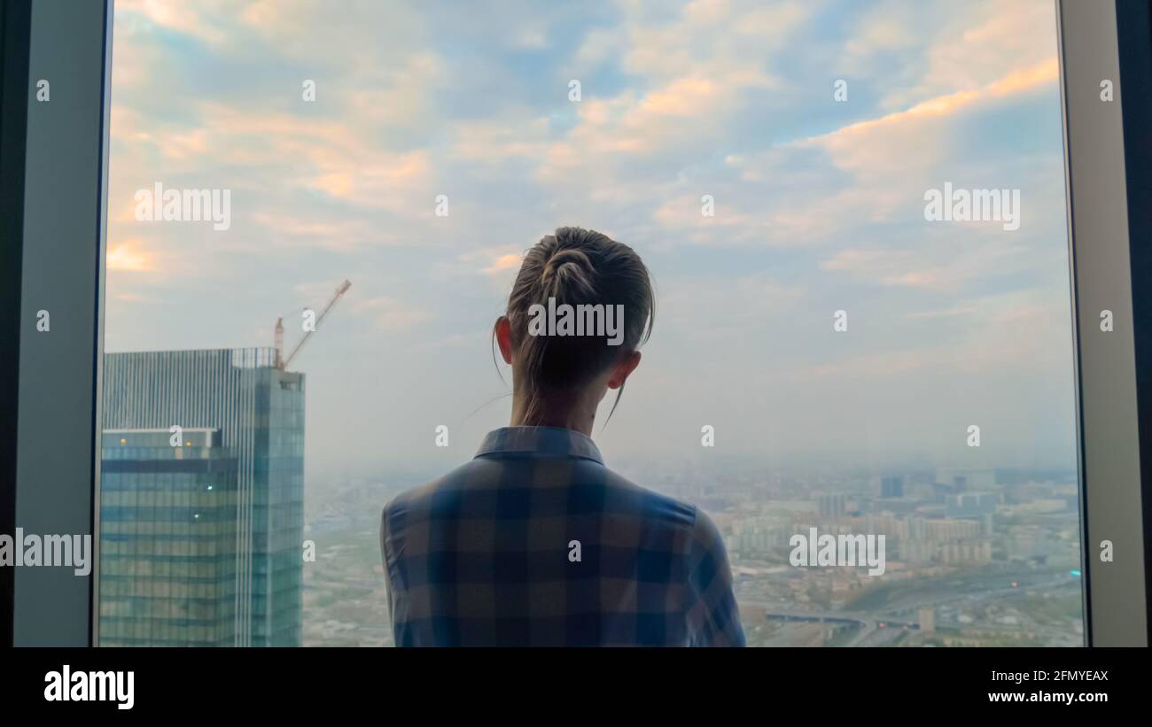 Back view of pensive woman looking at cityscape through window of ...