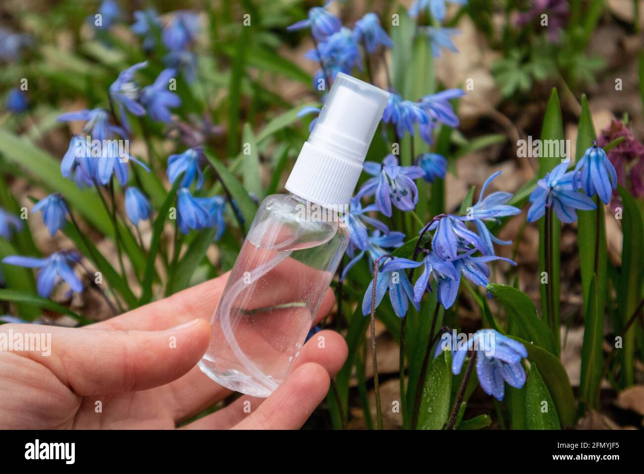 Hand holding clear liquid spray pump bottle in blooming pretty flower ...