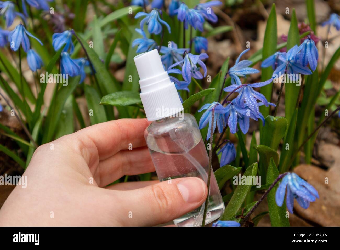 Hand holding clear liquid spray pump bottle in blooming pretty flower ...