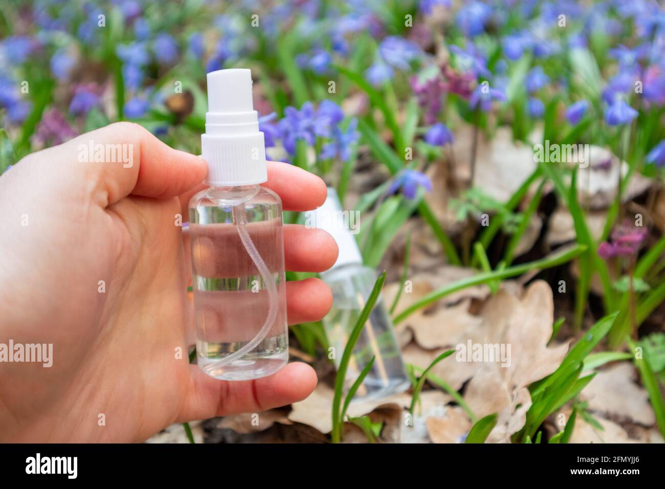 Hand holding clear liquid spray pump bottle in blooming pretty flower ...