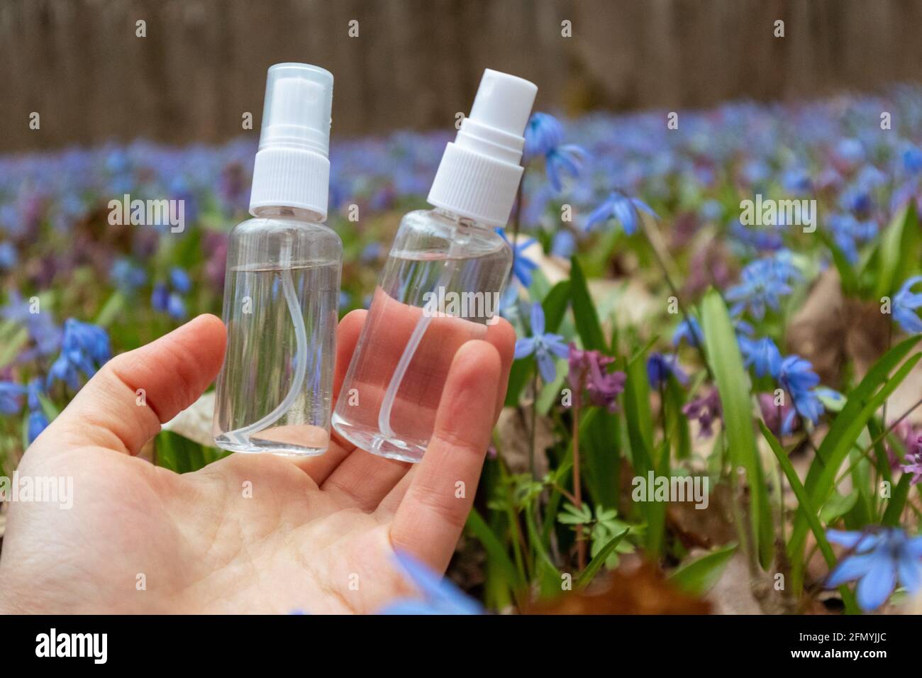 Hand holding two clear liquid spray pump bottles in blooming pretty ...