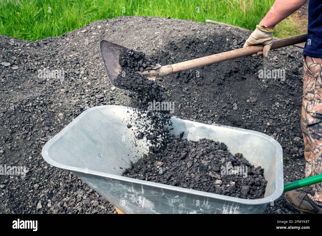 unidentified man pours gravel into a wheelbarrow. as part of a ...