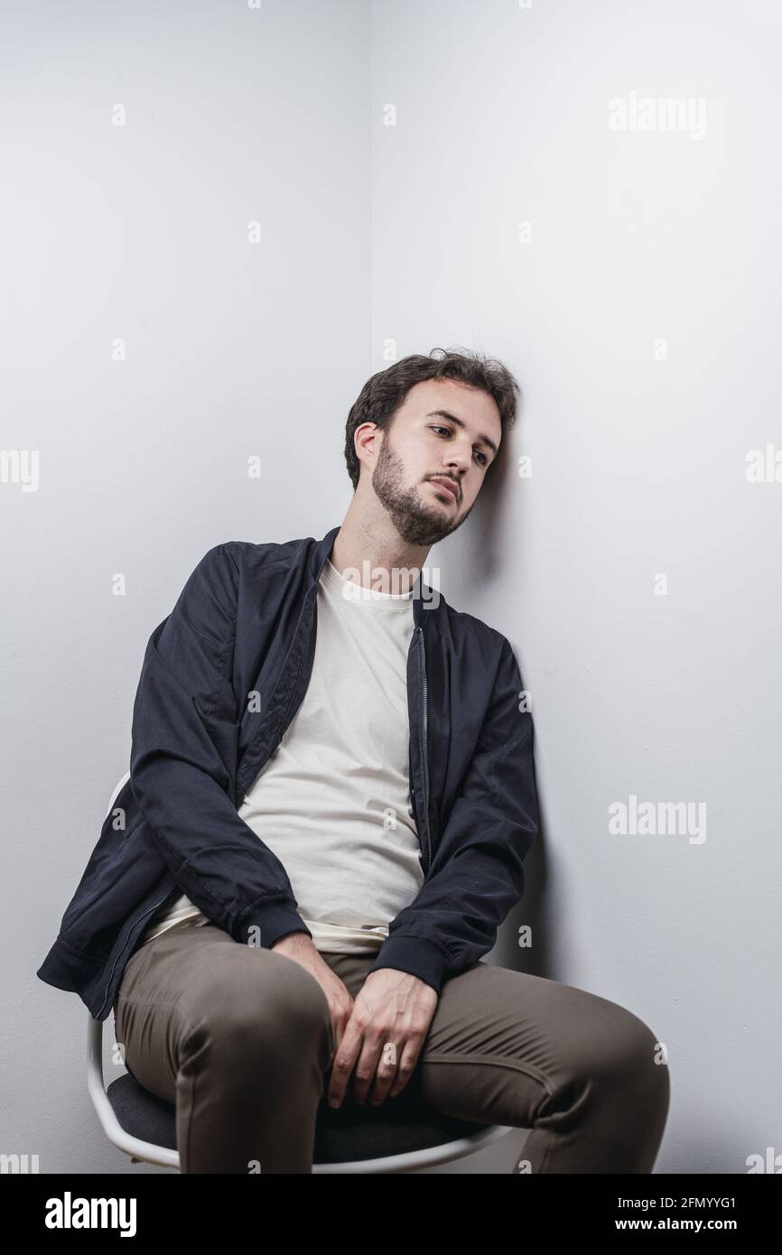 Depressed young Spanish male sitting on a chair leaning his head ...
