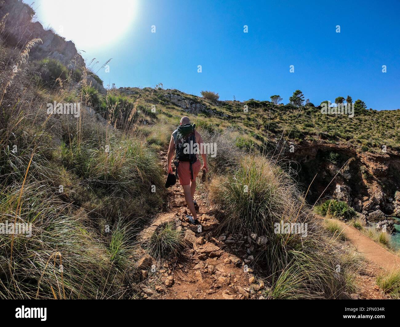 Back view of a male hiker climbing up the mountain with bright sun ...